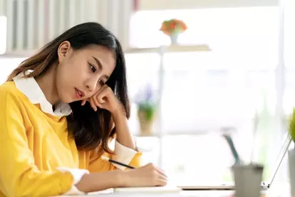 Jonge aantrekkelijke Aziatische vrouwelijke student zittend aan tafel denken en schrijven dagboek met de hand notitie ide...