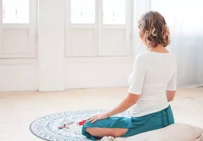 Vrouw mediteert het beoefenen van yoga voor kaarsen en rode rozenblaadjes, uitzicht vanaf de achterkant