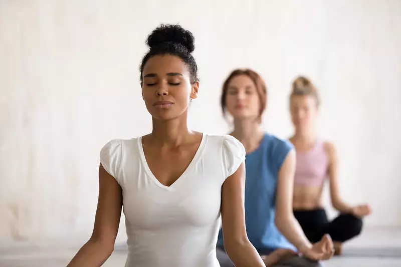 Gruppo diverse giovani belle donne sedute nella posizione del loto meditando durante la sessione allo yoga stud...