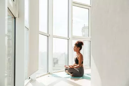 Ung afrikansk fitnessdam i sportkläder som sitter i lotusställning och tittar på kameran hemma