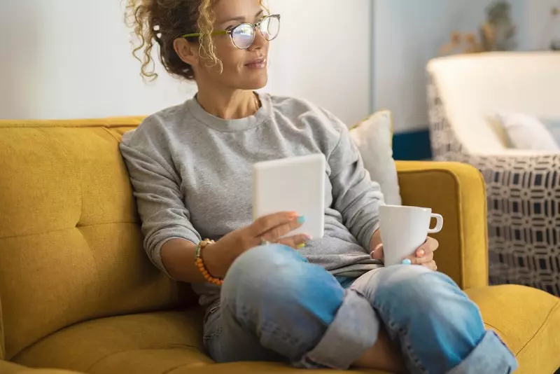 Una dona s'asseu al sofà amb una tassa de cafè mentre pren un descans d'Instagram.