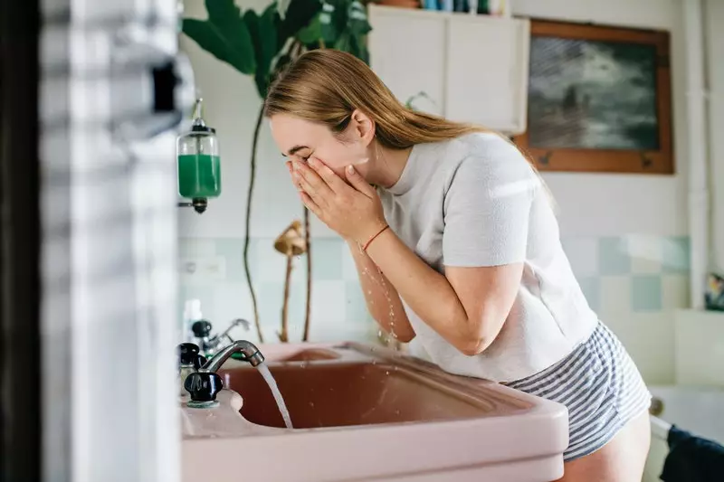 Žena se skláněla nad umyvadlem a myla si obličej.