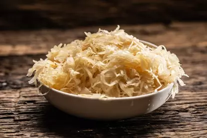 Isang mangkok na puno ng hilaw na sauerkraut cabbage pickle sa isang simpleng madilim na ibabaw.