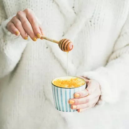 Sund vegansk gurkemeje latte eller gylden mælk med honning i kvindelige hænder, firkantet afgrøde