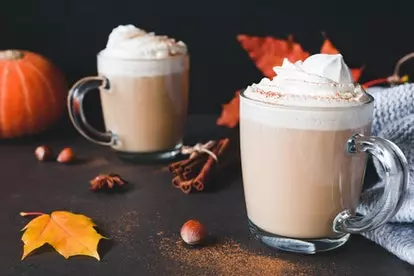 Varm chokolade med flødeskum og kanel eller Pumpkin Spice Latte med creme i krus på mørk bagside...